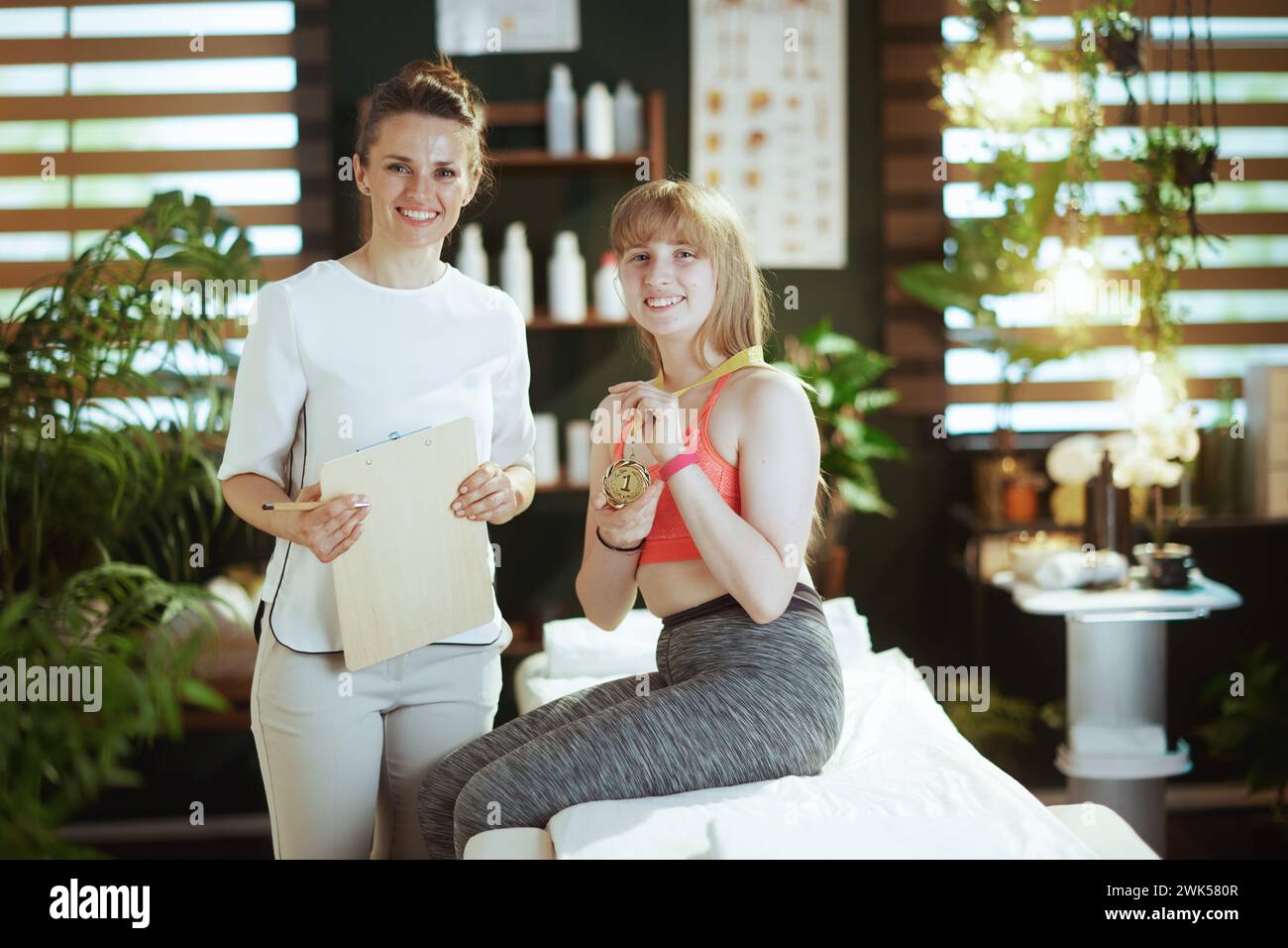 Healthcare time. happy female massage therapist in massage cabinet with clipboard, teenage ...