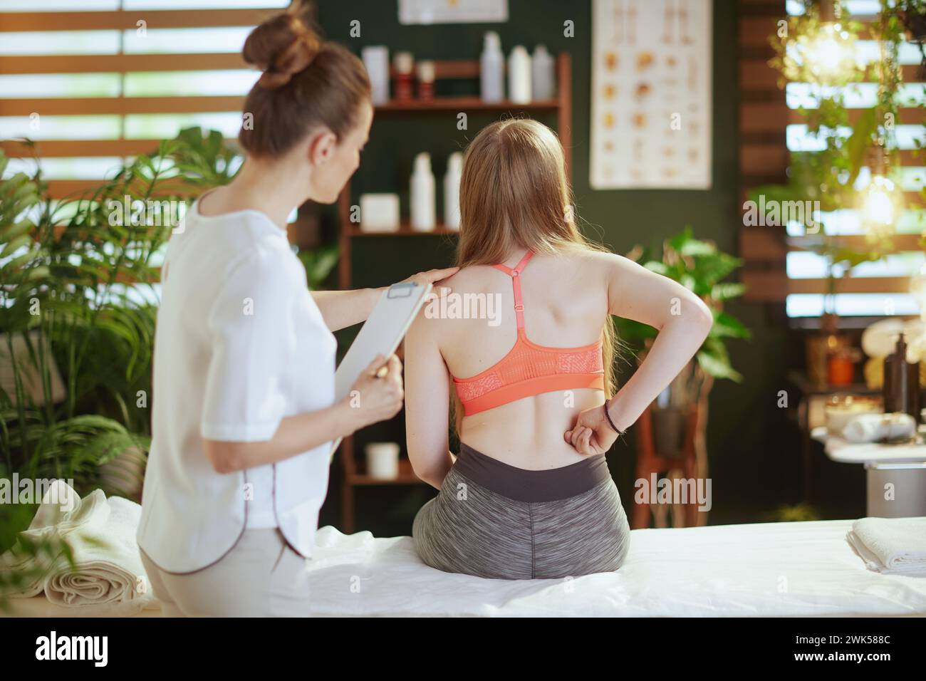 Healthcare time. Seen from behind female medical massage therapist in massage cabinet with ...