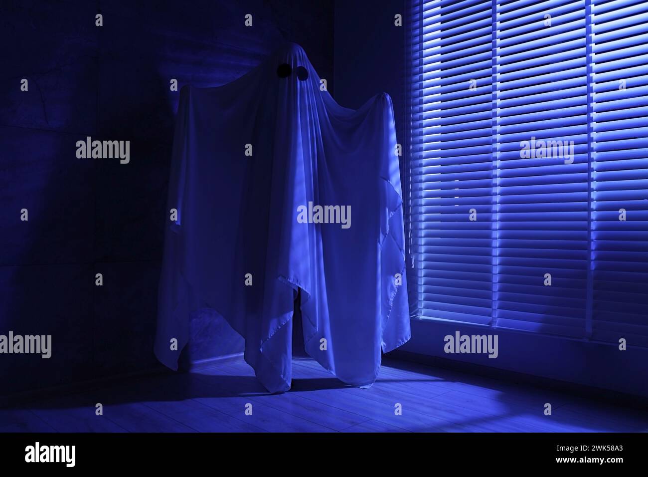Creepy ghost. Woman covered with sheet near window in blue light Stock ...