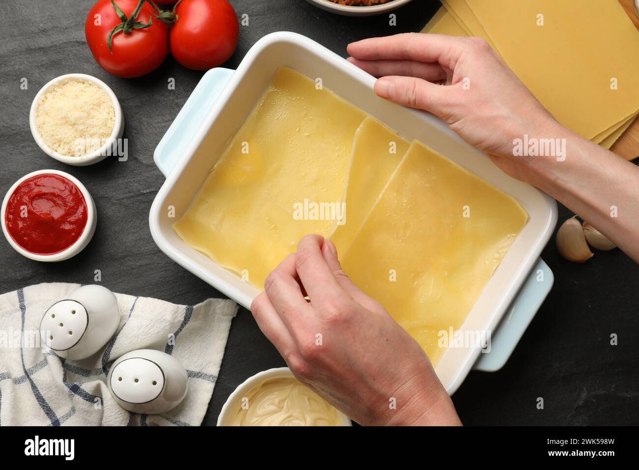 Woman making lasagna at dark table, top view Stock Photo - Alamy