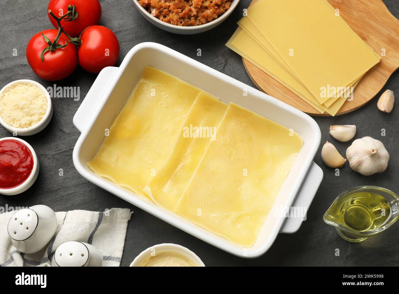 Cooking lasagna. Pasta sheets in baking tray and products on dark ...