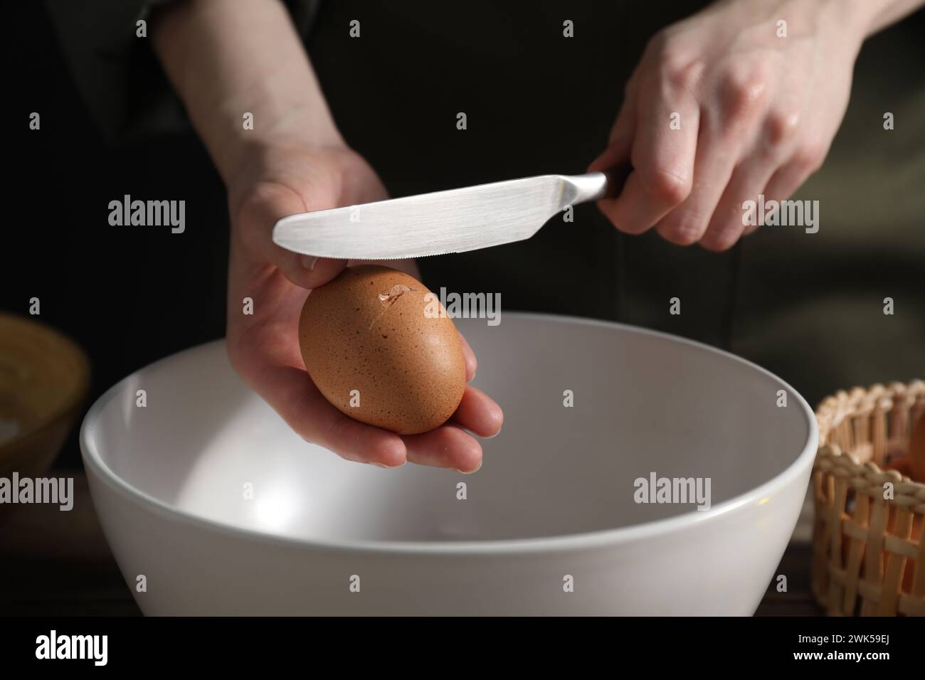 Making bread. Woman adding egg into dough at wooden table on dark background, closeup Stock ...