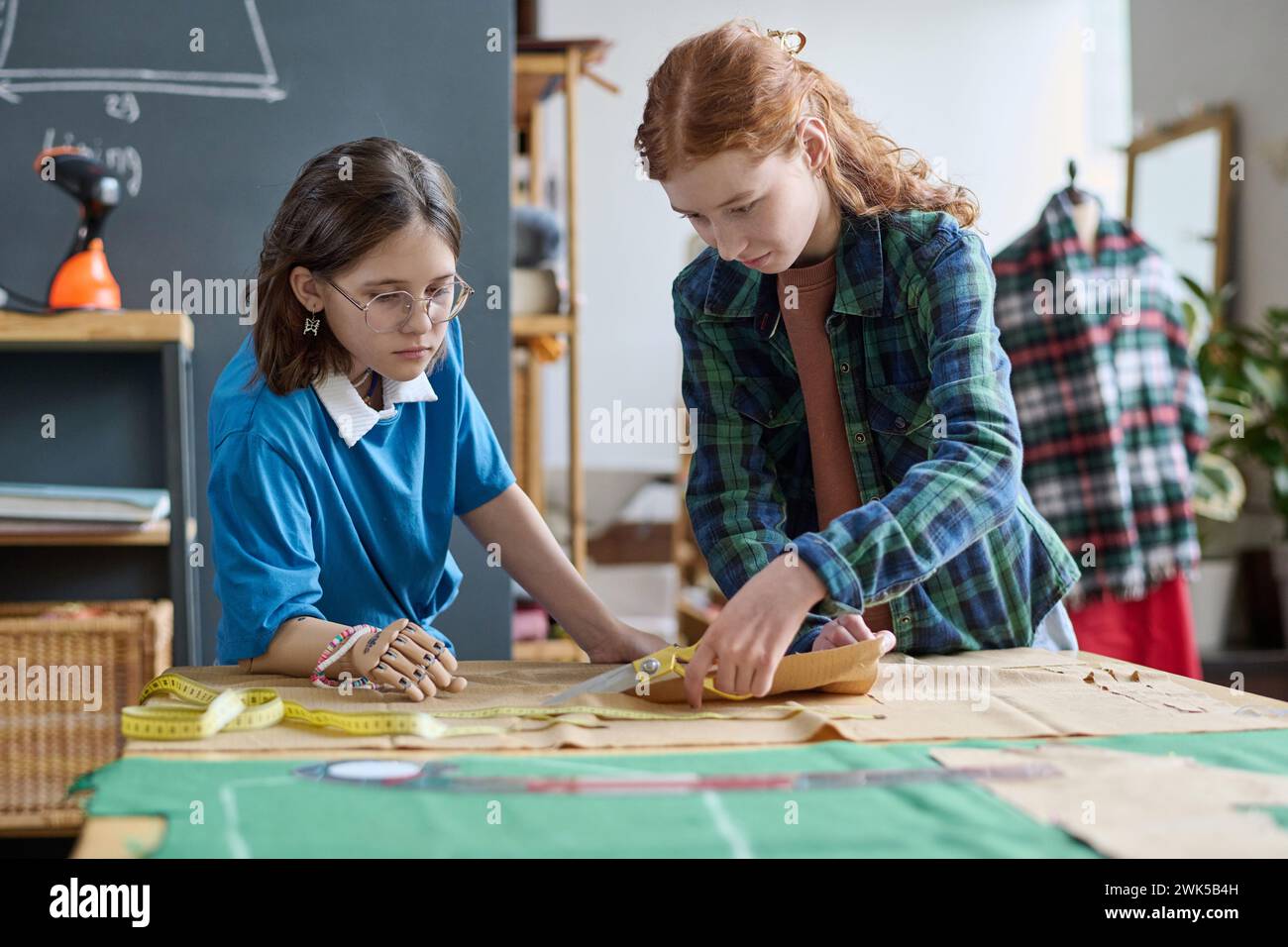 Portrait of two teen girls making clothing patterns together in sewing ...