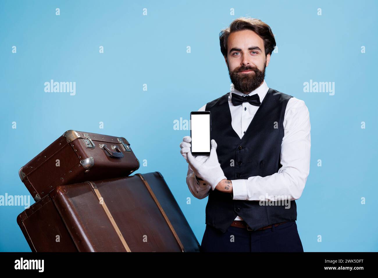Stylish bellboy uses mobile phone with white display, holding device in ...