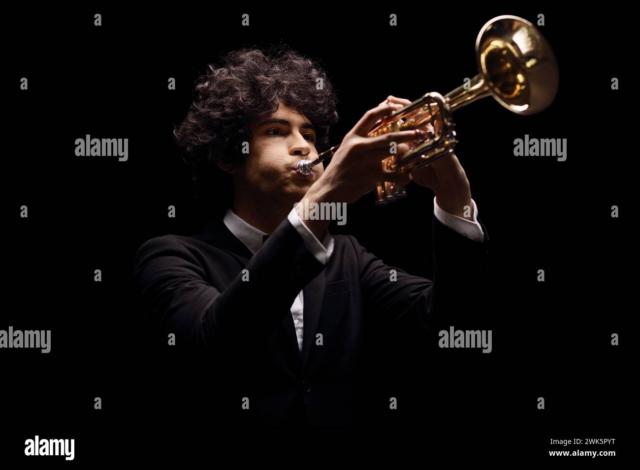 Young man in a black suit playing a trumpet isolated on black ...