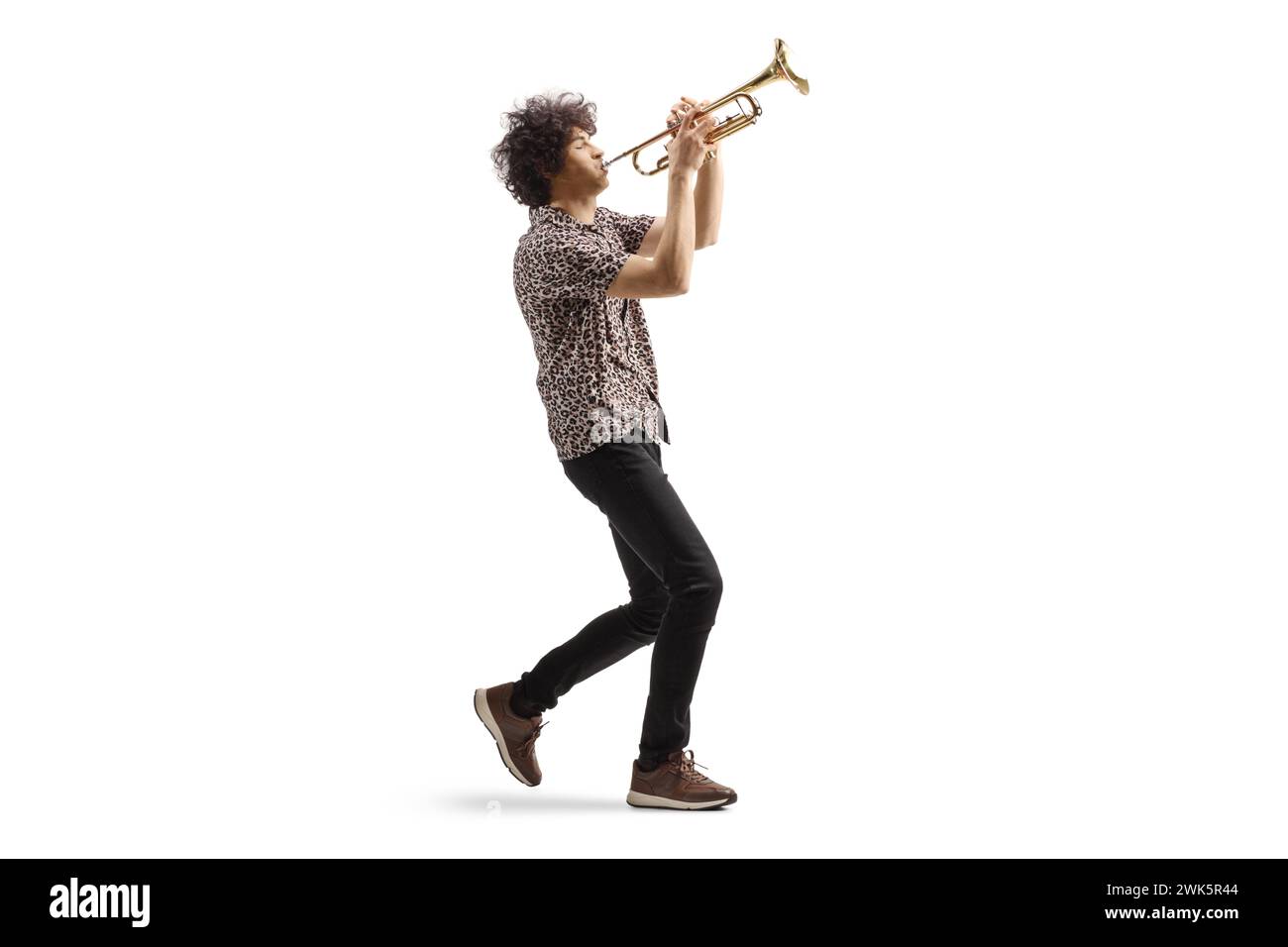 Full length profile shot of a young man walking and playing a trumpet ...
