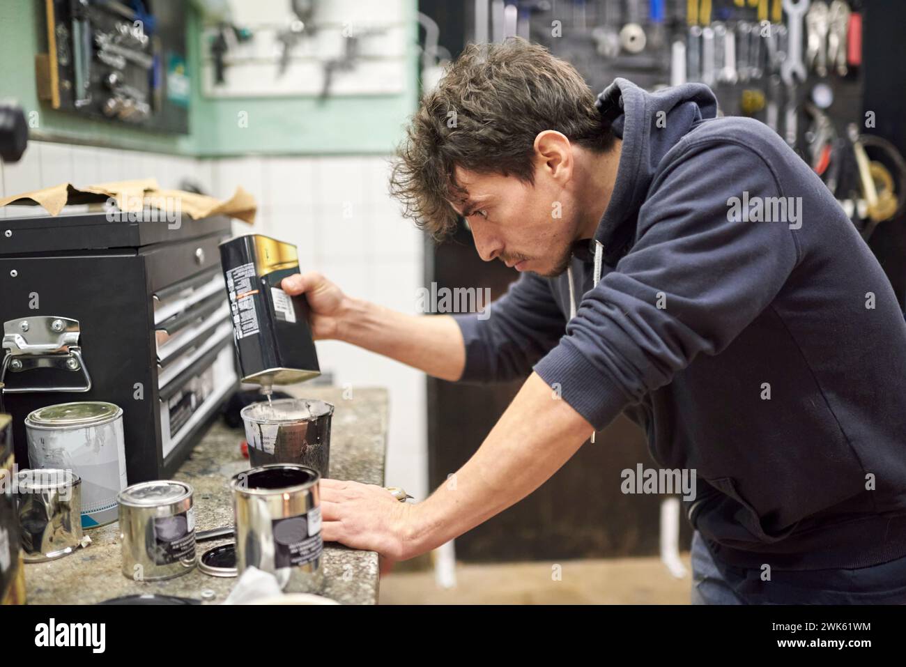 Young hispanic man pouring thinner into a cup of black paint on a ...