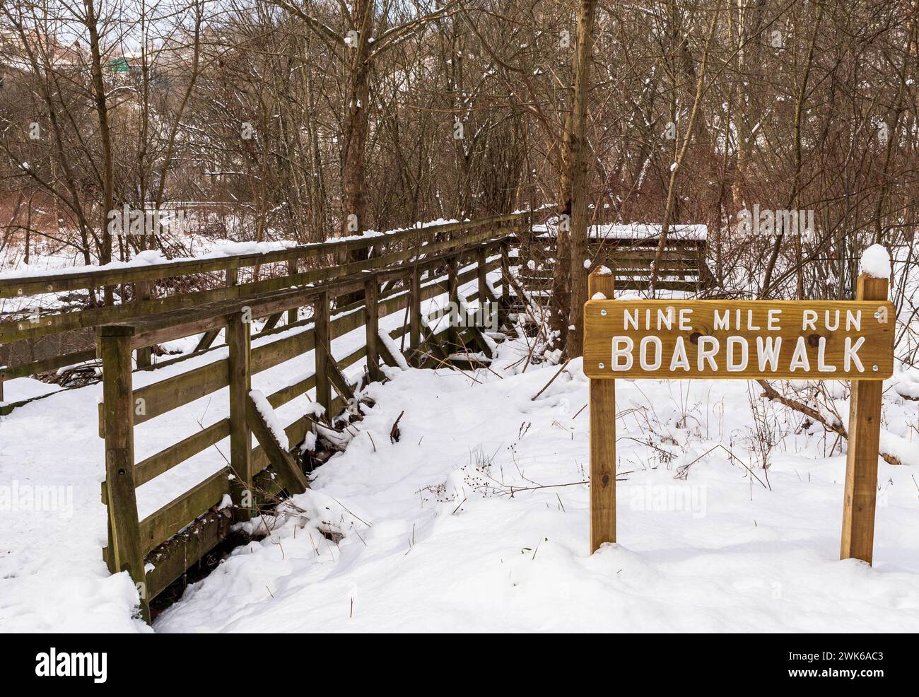 A wooden sign engraved with Nine Mile Run Boardwalk, a stream and ...