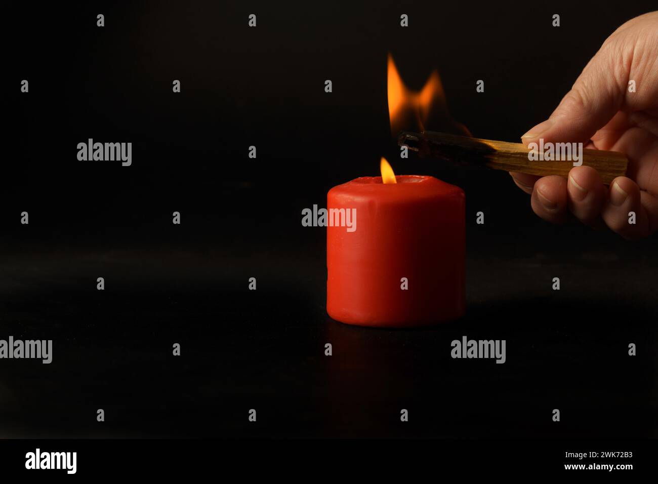 A woman lights a holy stick, palo santo, with a red candle flame ...