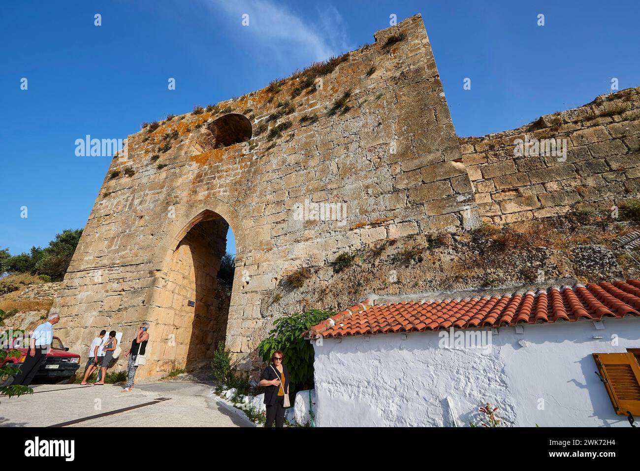 Visitors stroll next to an ancient masonry arch under a blue sky ...