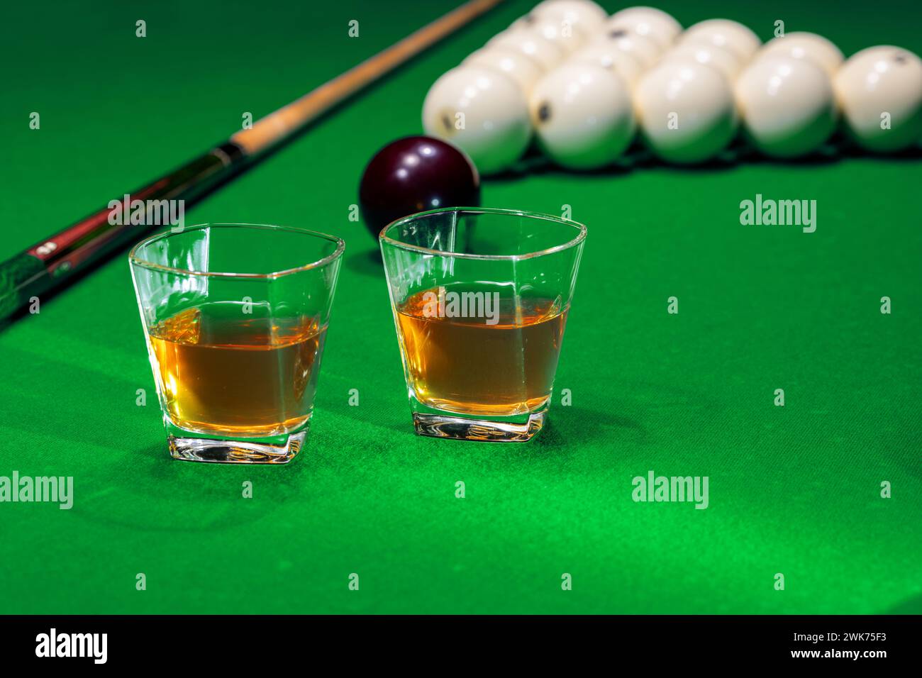 Two glass of whiskey on billiard table with cue and billiard balls in ...
