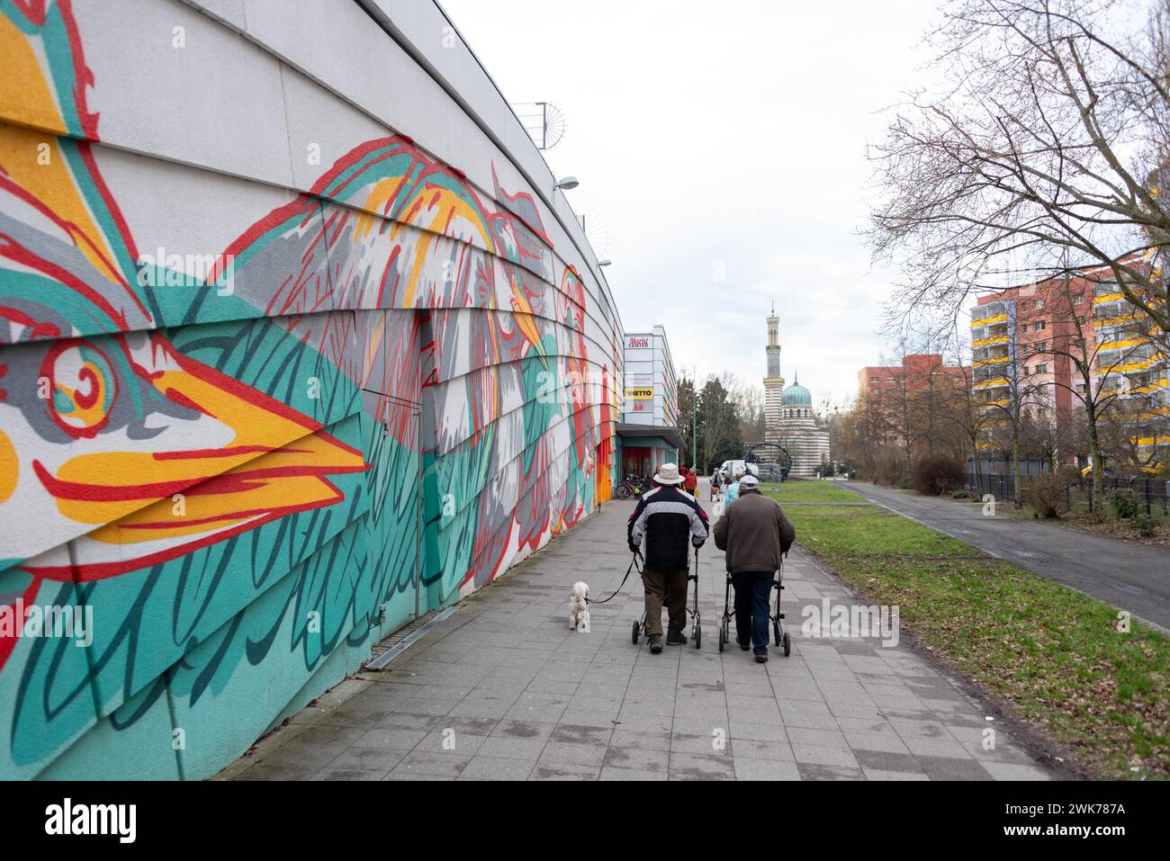 People with a dog walk past a colourful wall graffiti in front of ...