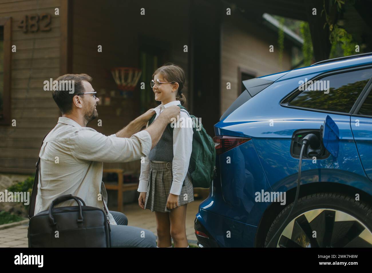 Portrait of a man charging electric car in front of his house.Man is unplugging charger from the ...