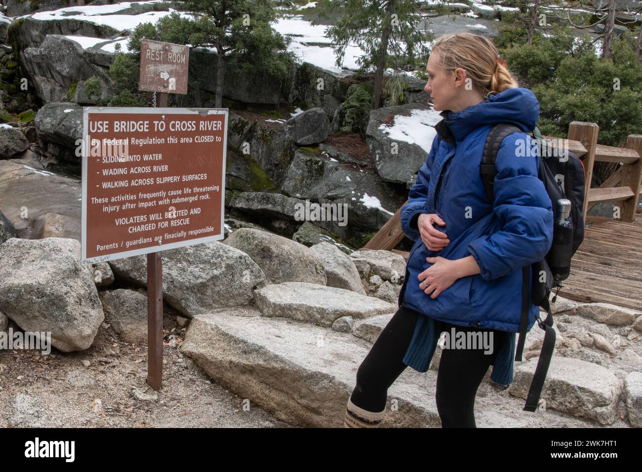 A female hiker reads a cautionary trail sign about bridge usage and ...