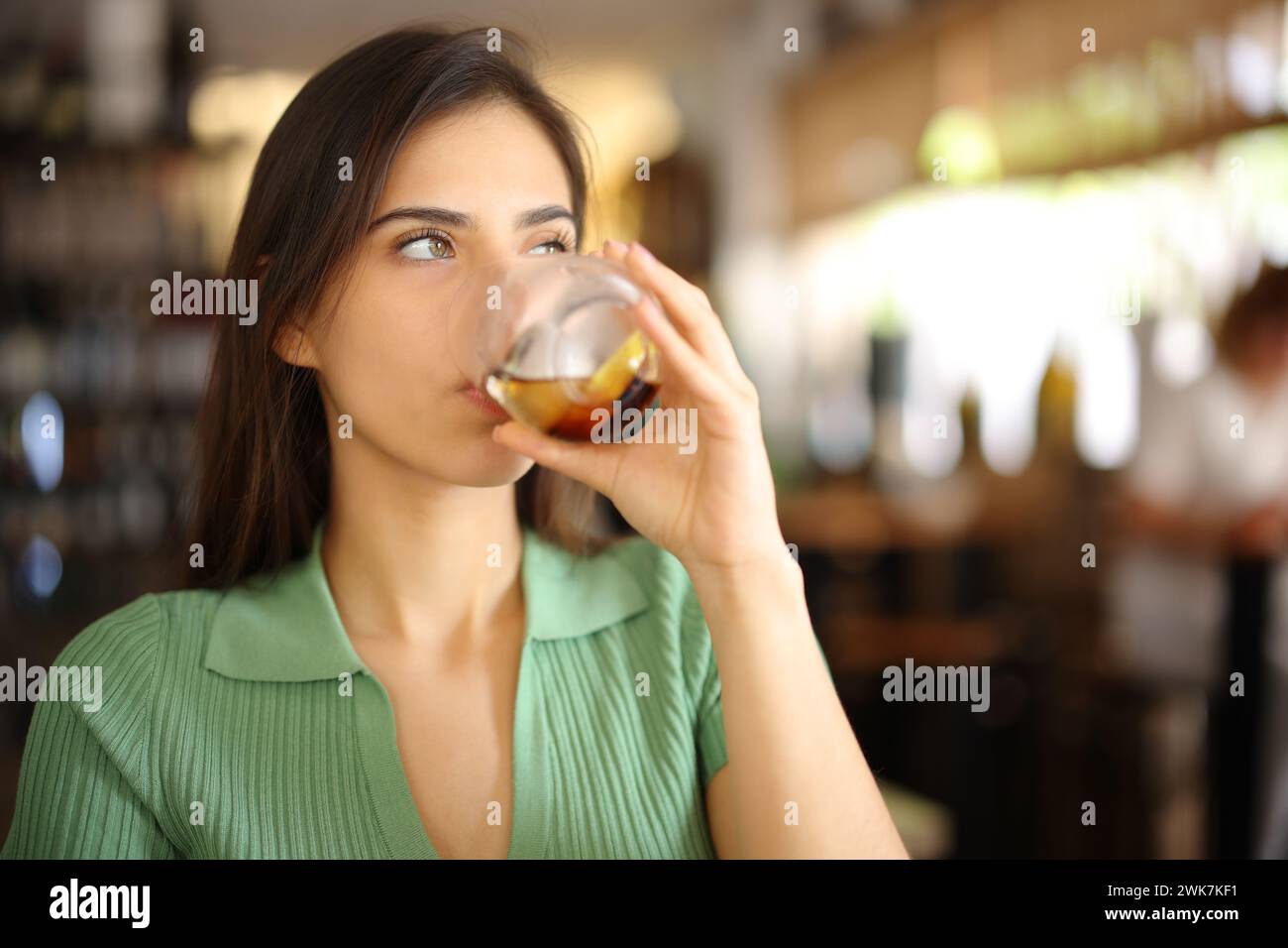 Serious woman drinking soda in a restaurant interior looking at side ...