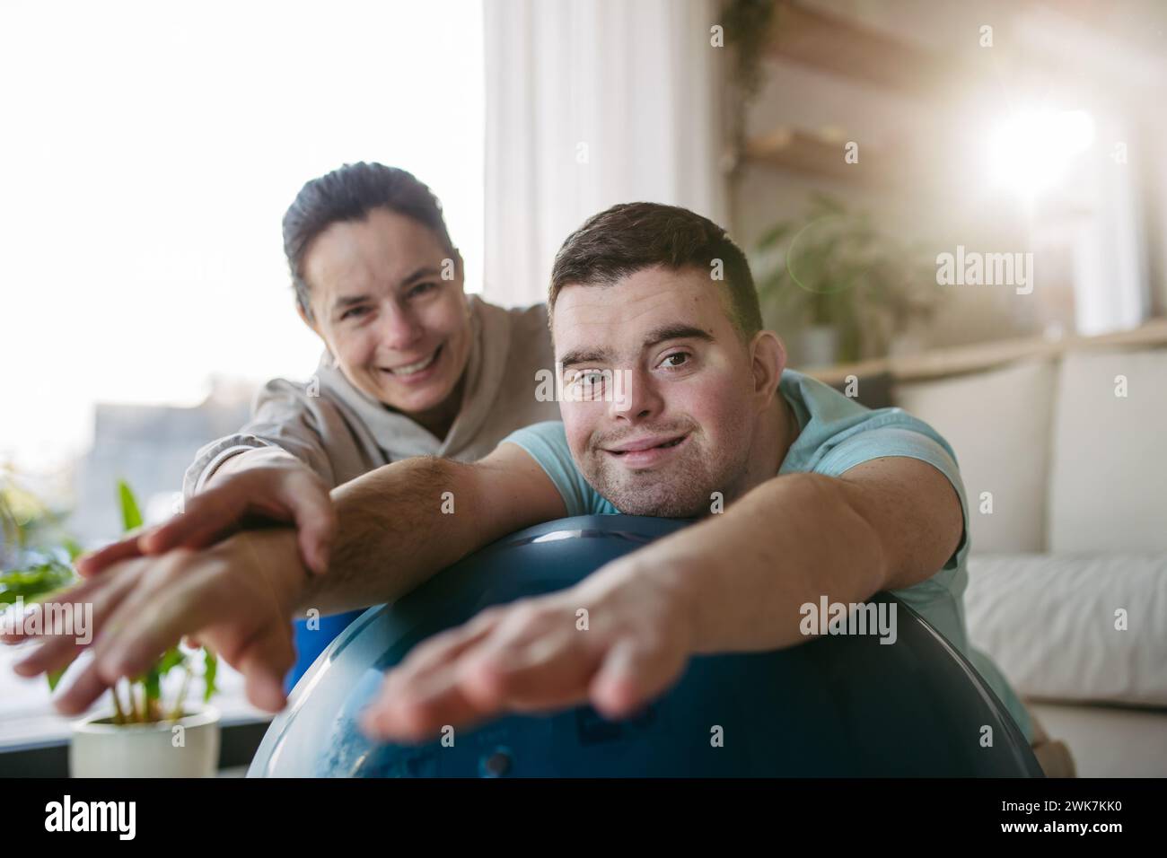 Young man with Down syndrome exercising at home with his mother on a ...