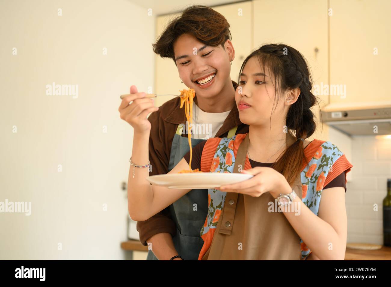 Romantic couple in aprons tasting spaghetti pasta while preparing food ...