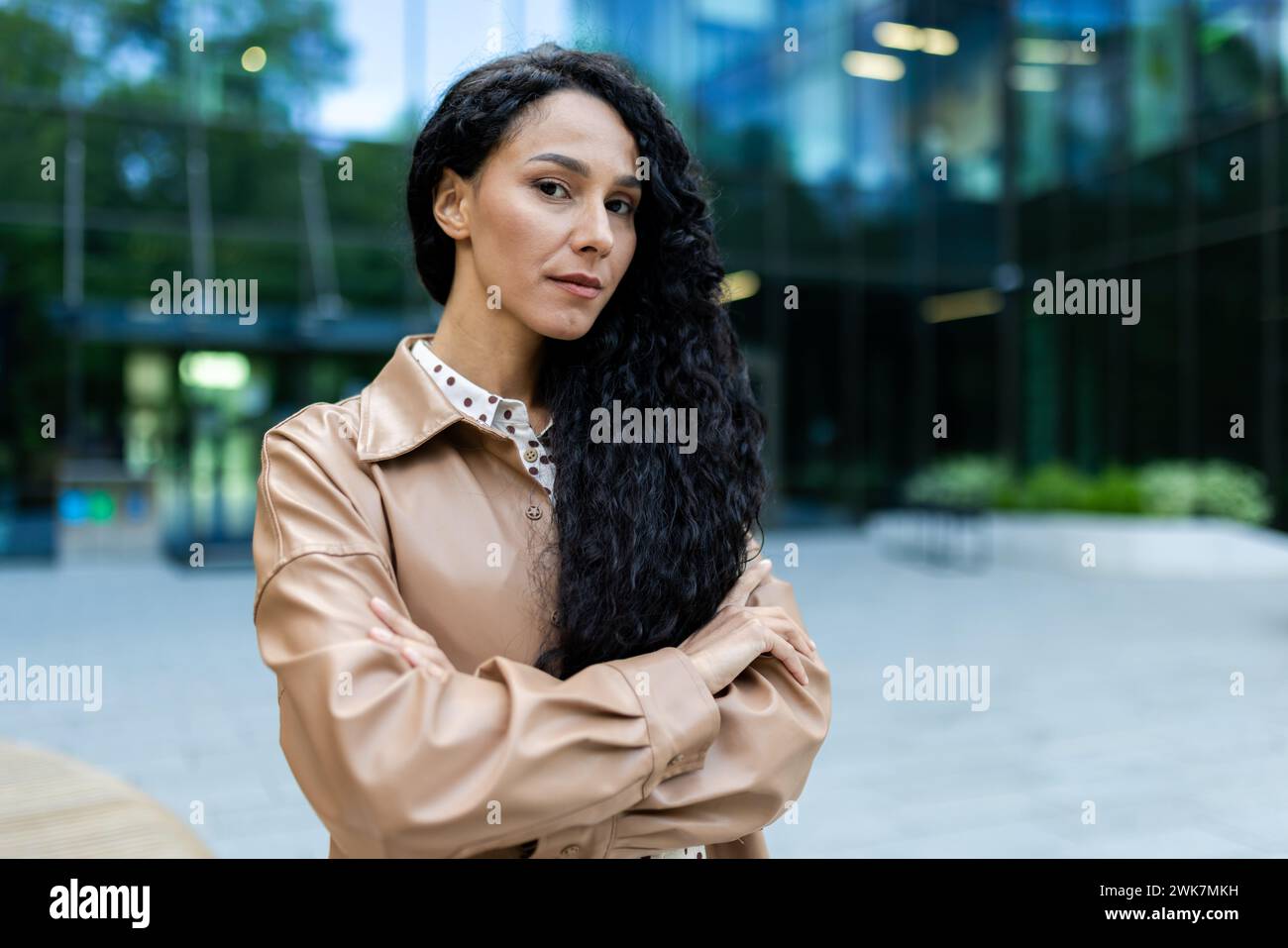 Elegant businesswoman with curly hair crossing arms during a work break ...