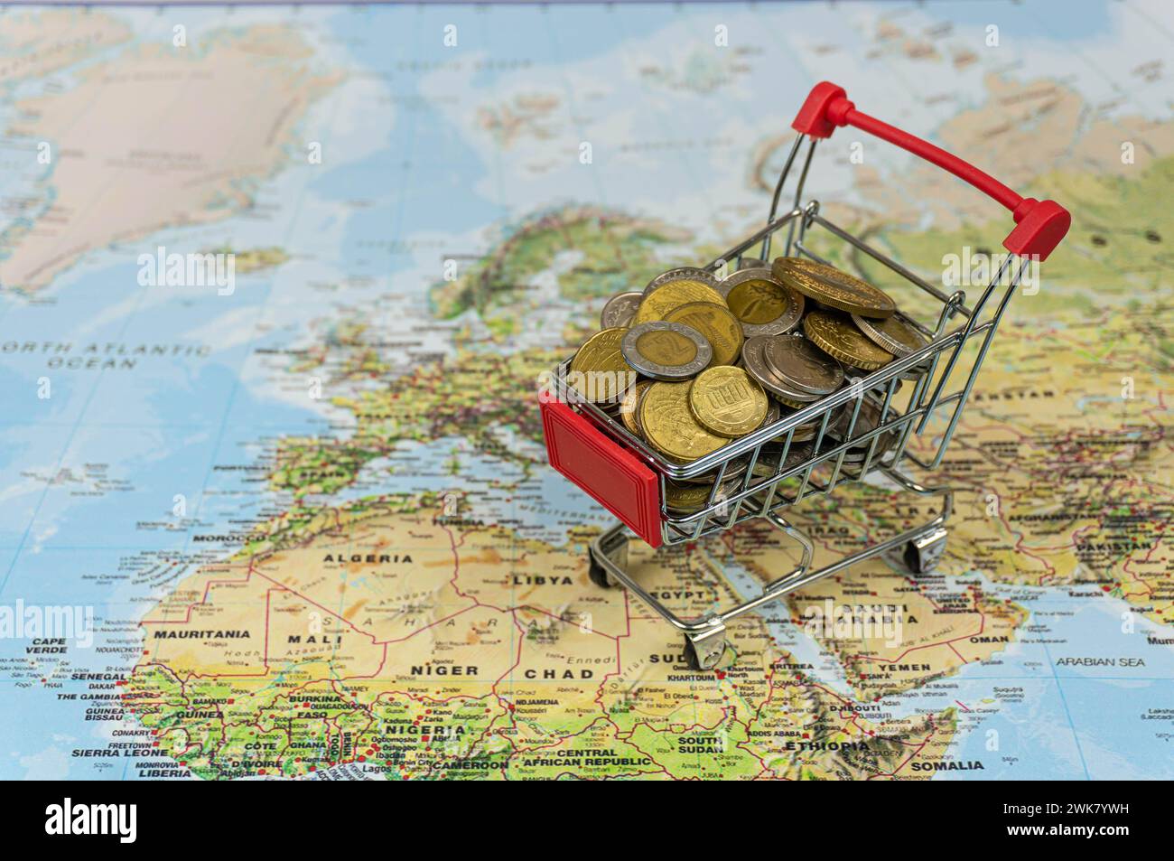 A supermarket cart full of coins. On the background is a map of the ...
