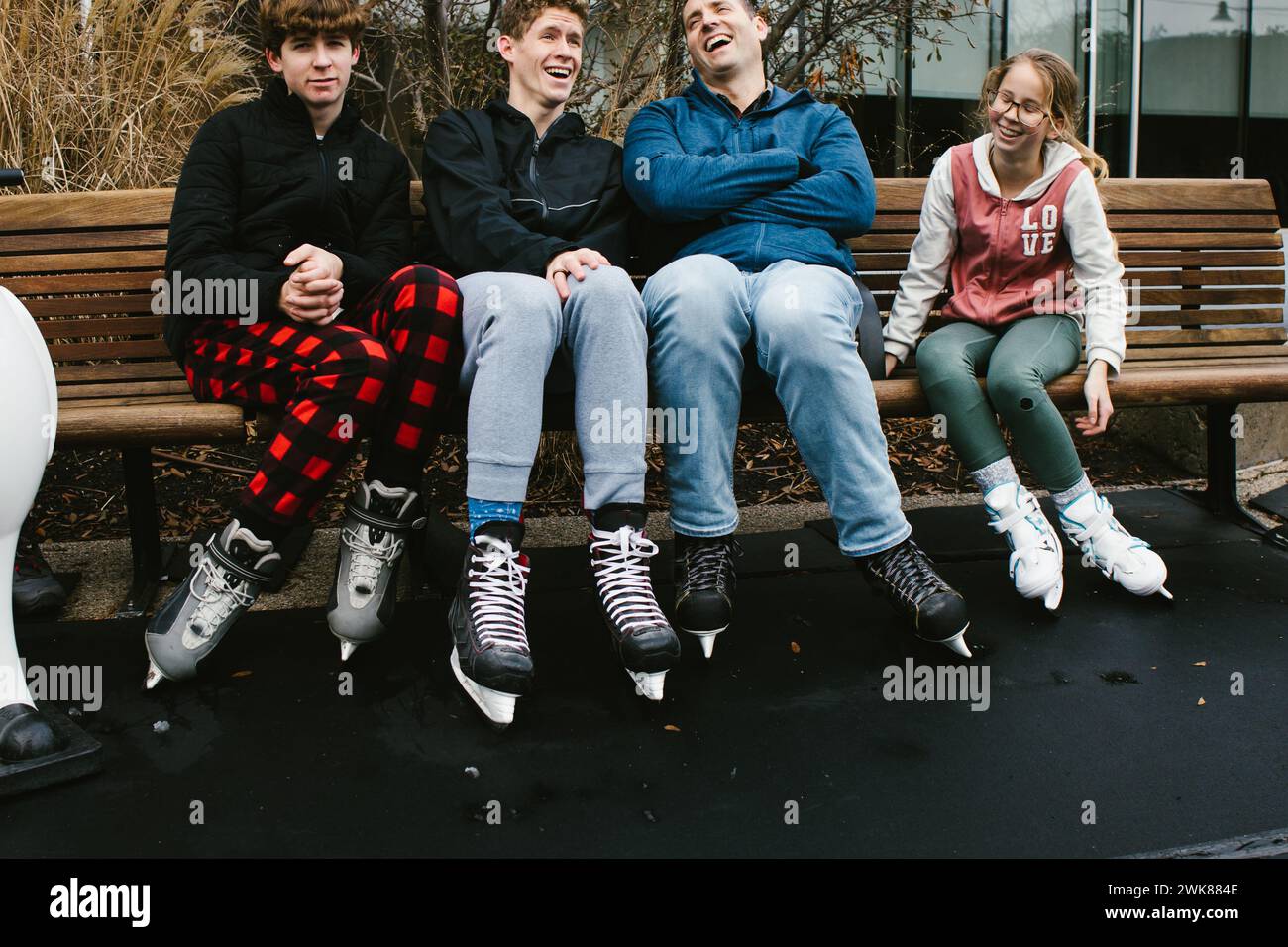 Siblings and Dad laugh together on bench during ice skating break Stock ...