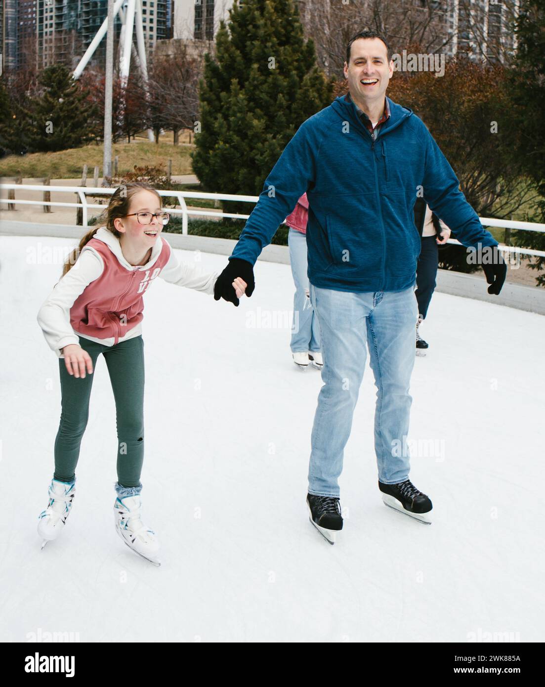 Father and daughter holding hands ice skating in city together Stock ...