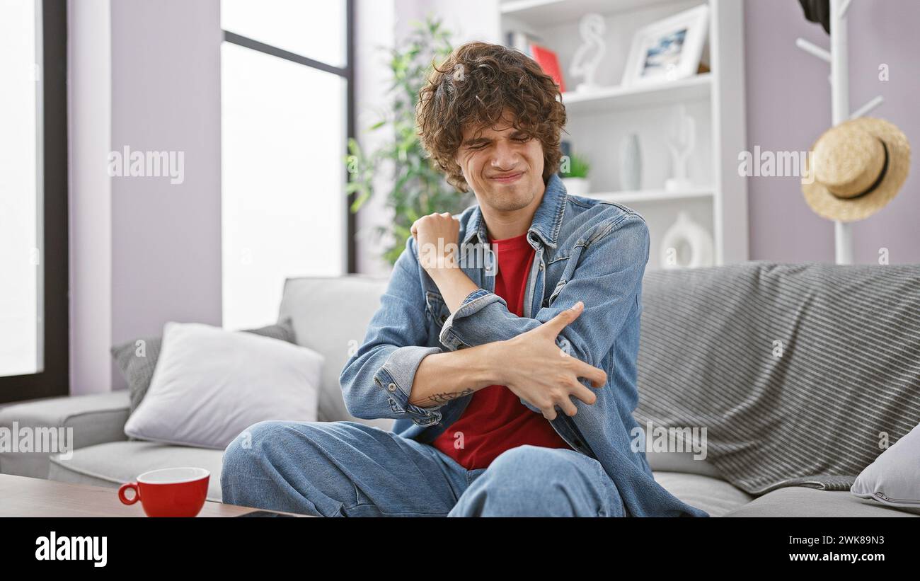 A young man winces in pain, clutching his elbow in a modern living room ...