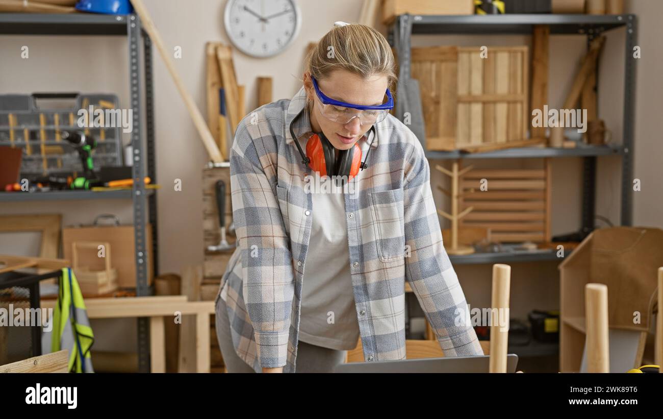 Focused blonde woman wearing safety goggles works at carpentry bench in ...