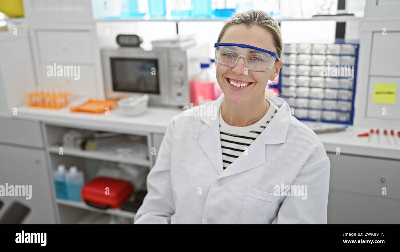 Smiling young caucasian woman in white lab coat and safety glasses ...