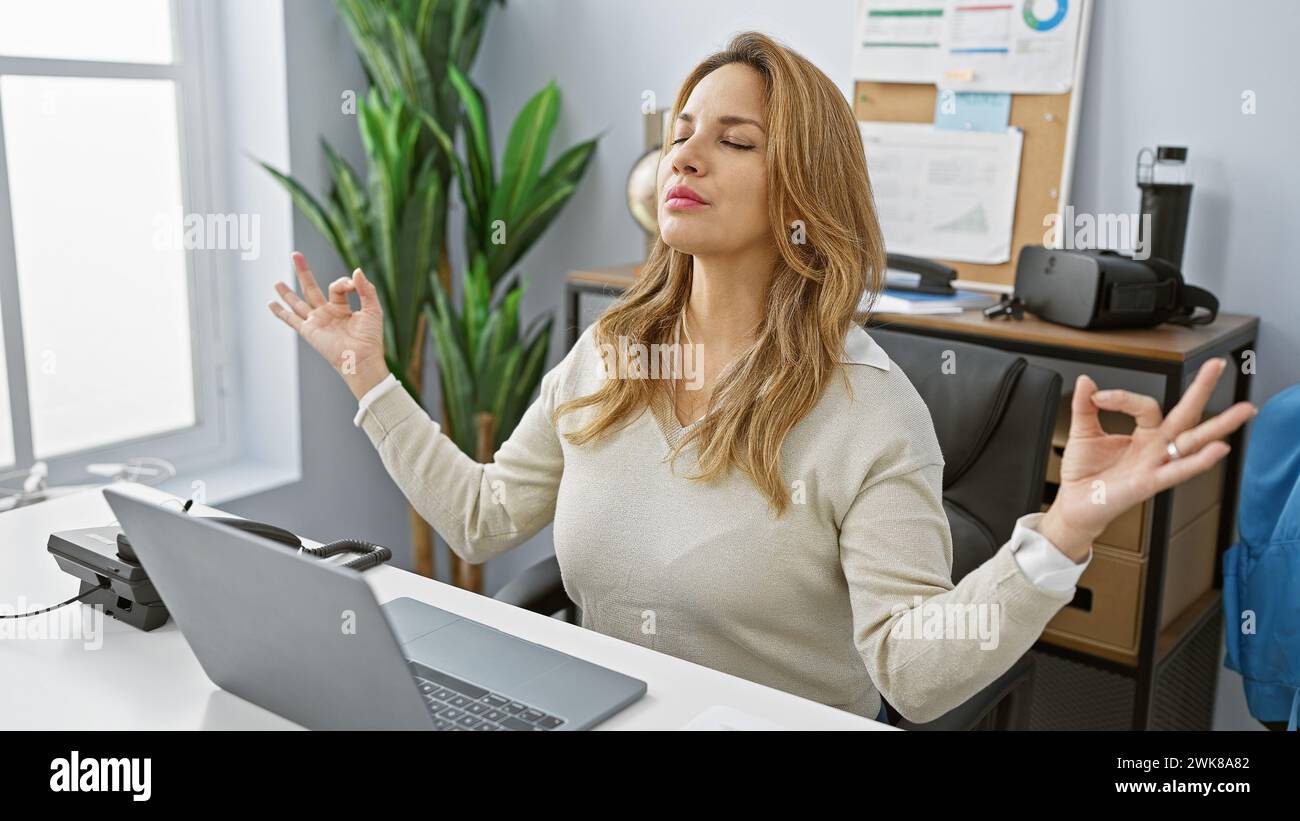 A relaxed hispanic woman meditates in her office, portraying ...