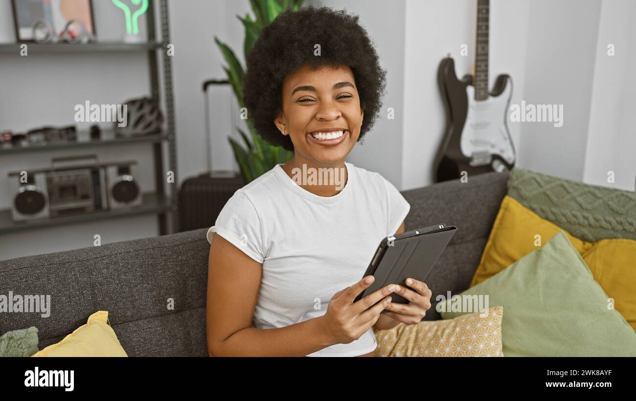 Smiling african american woman with curly hair using tablet indoors on ...
