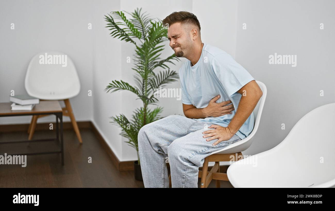 Young hispanic man with beard grimacing in pain, holding his stomach ...