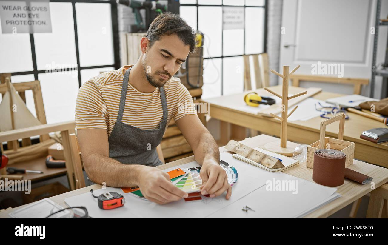 A focused hispanic man examines color swatches in a well-lit carpentry ...