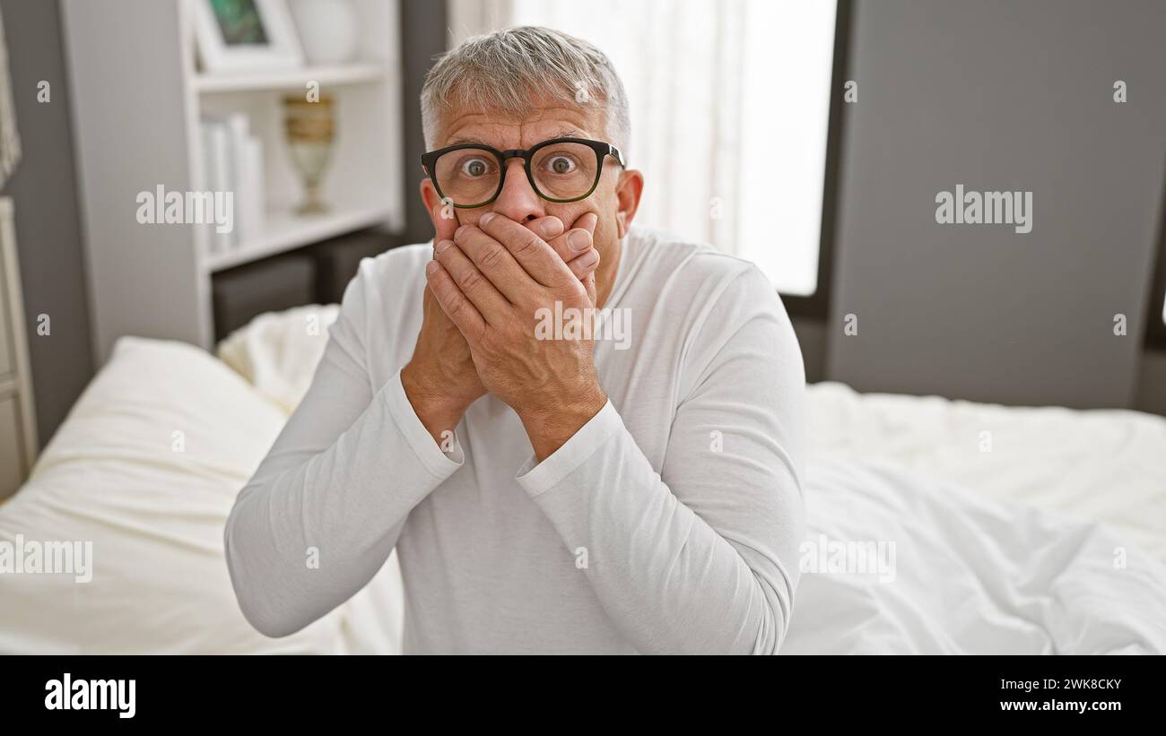 Shocked senior man covering mouth with hands in a white bedroom Stock ...