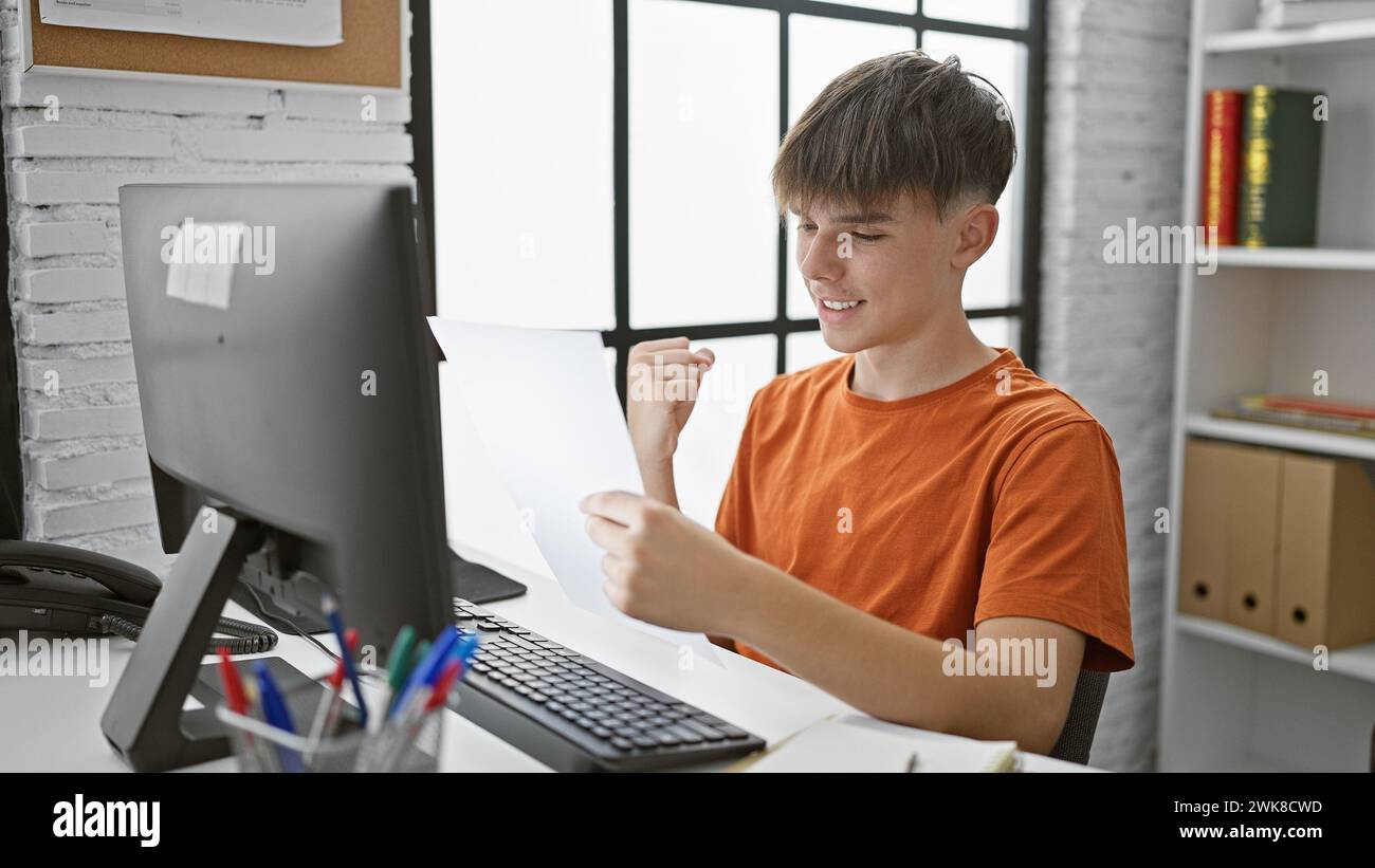 A pleased teenage boy celebrates academic success at a computer desk in ...