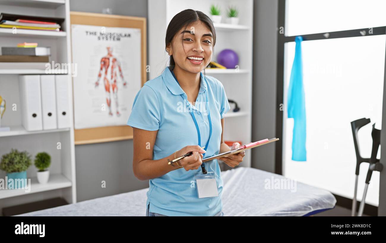 A smiling young indian woman with long hair, dressed in medical scrubs ...