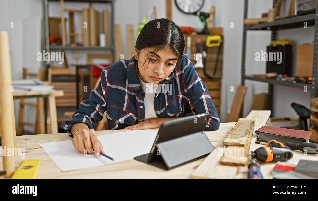 A focused indian woman drafts plans in a carpentry workshop surrounded ...