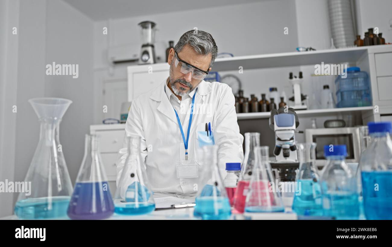 Handsome, grey-haired young hispanic male scientist seriously focused on medical experiment ...