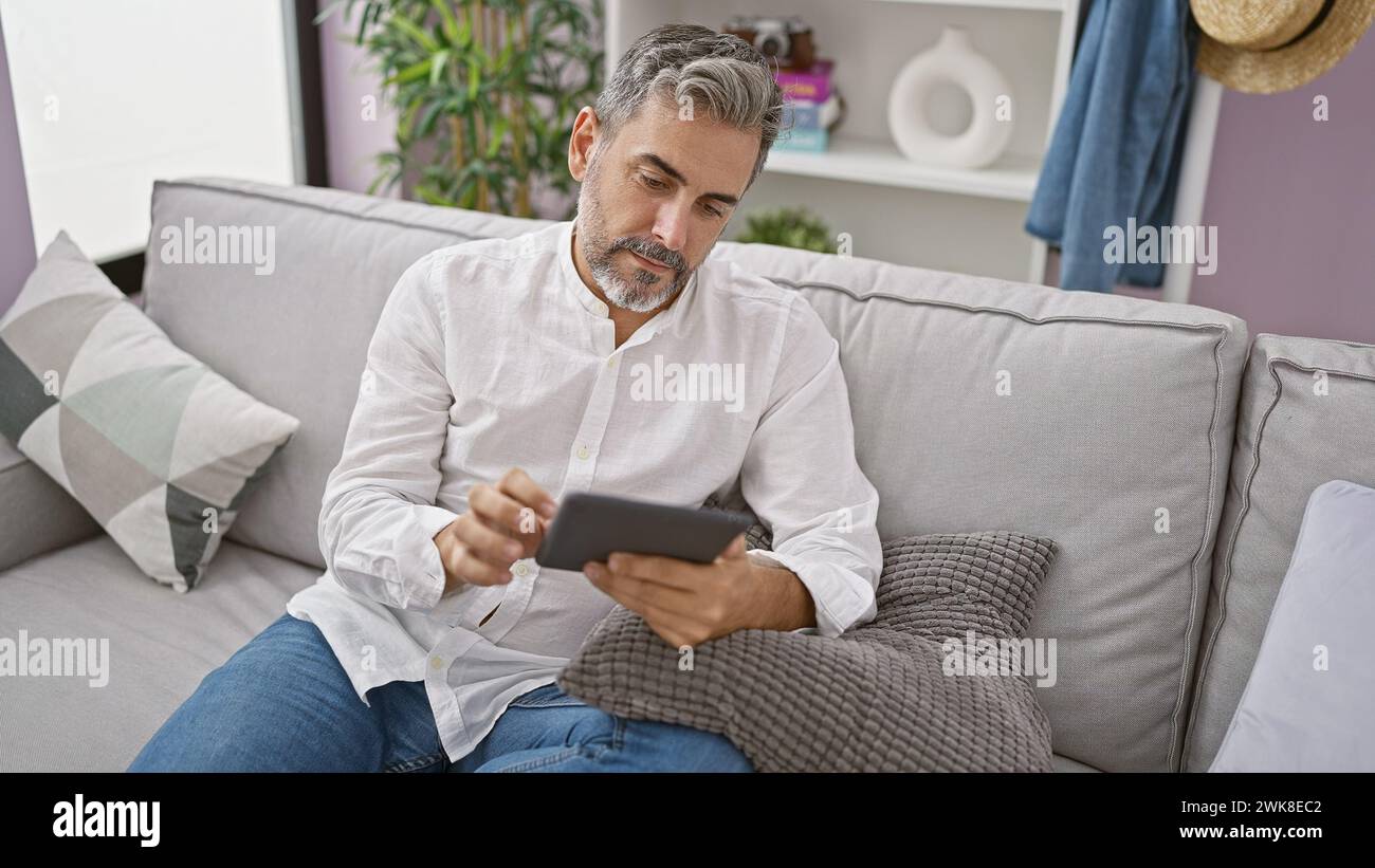 Handsome young hispanic man with grey-haired beard, relaxing at home ...