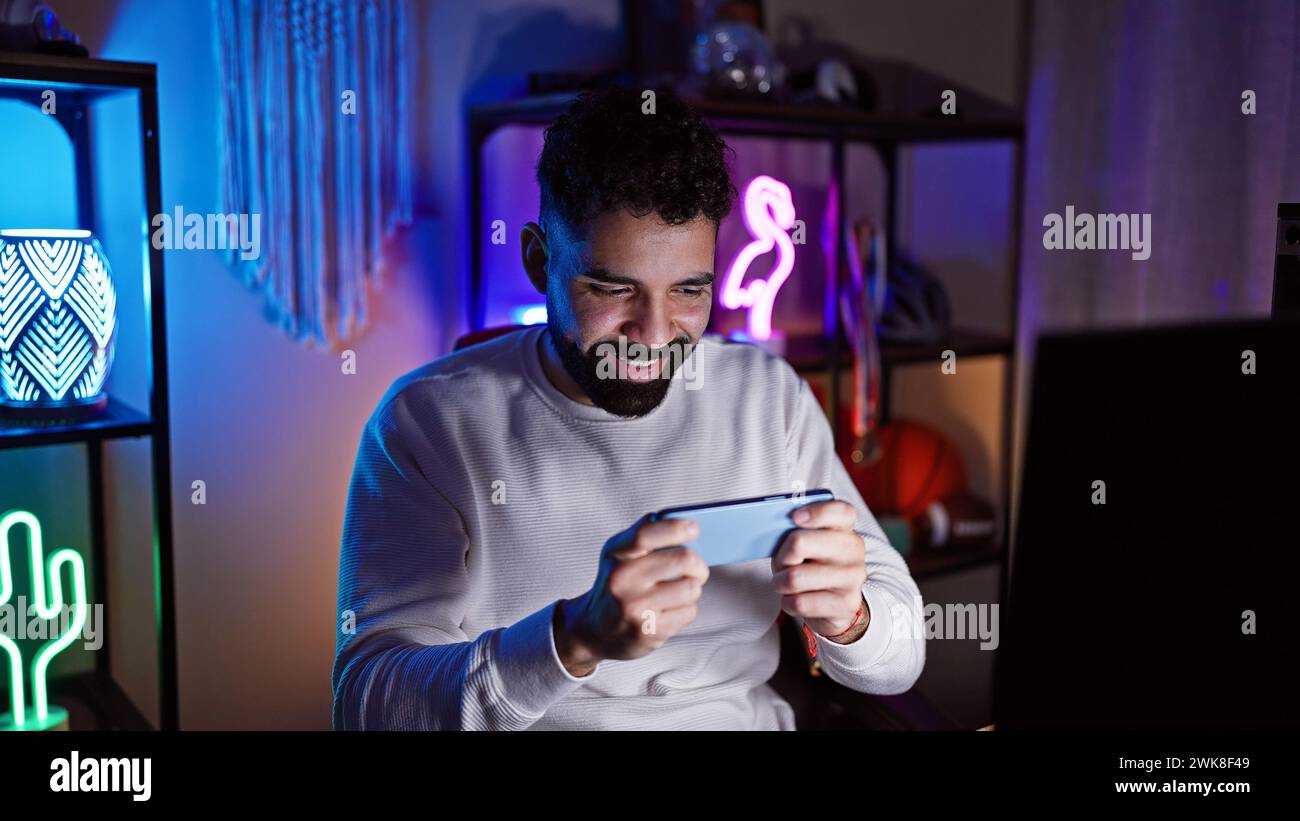 Happy man gaming on smartphone in a colorful neon-lit room at night ...