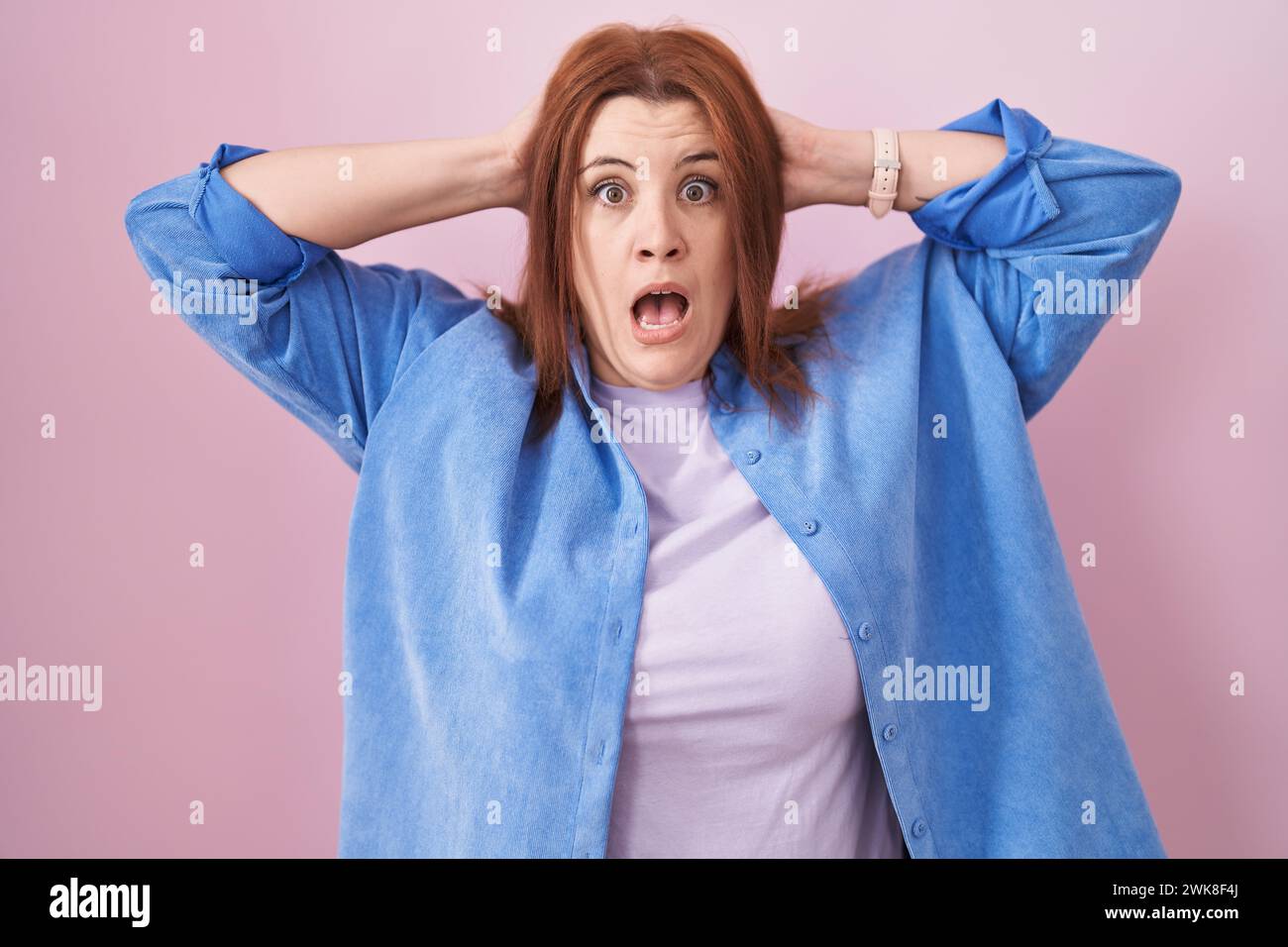 Young hispanic woman with red hair standing over pink background crazy ...