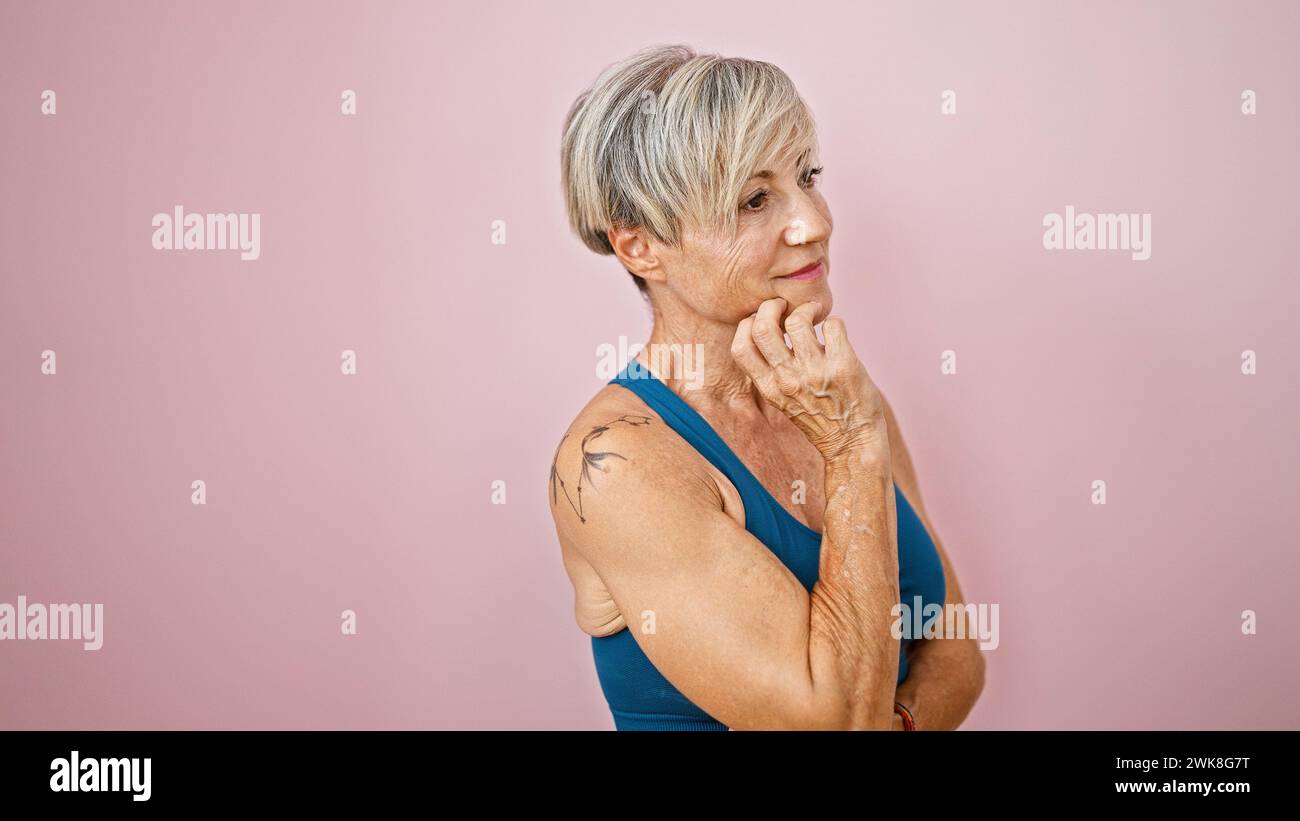 A thoughtful mature woman with grey short hair posing against a pink ...