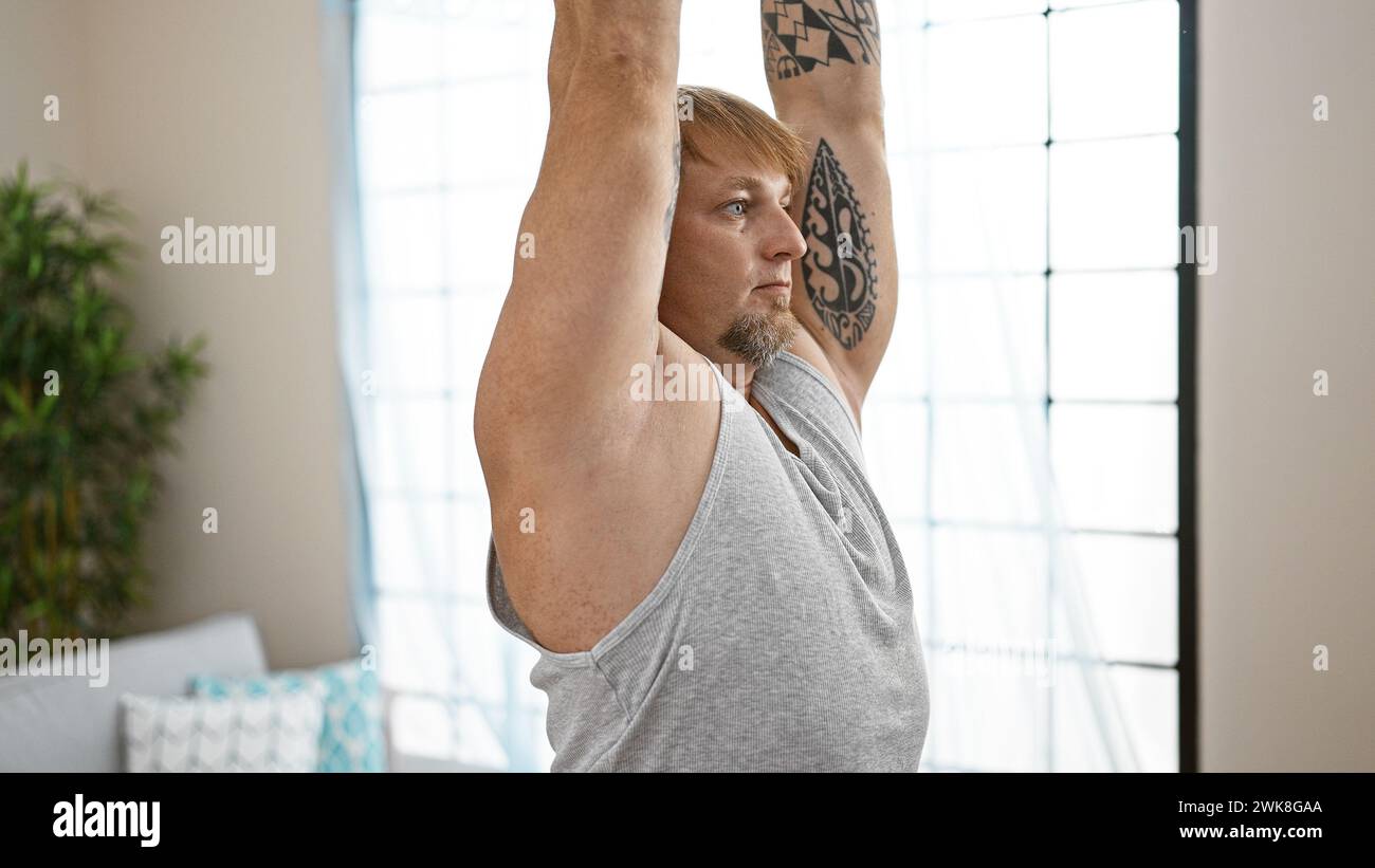A tattooed man stretches in a well-lit living room, displaying health ...
