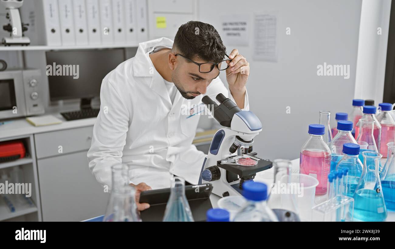 A man in a lab examines samples through a microscope surrounded by test ...