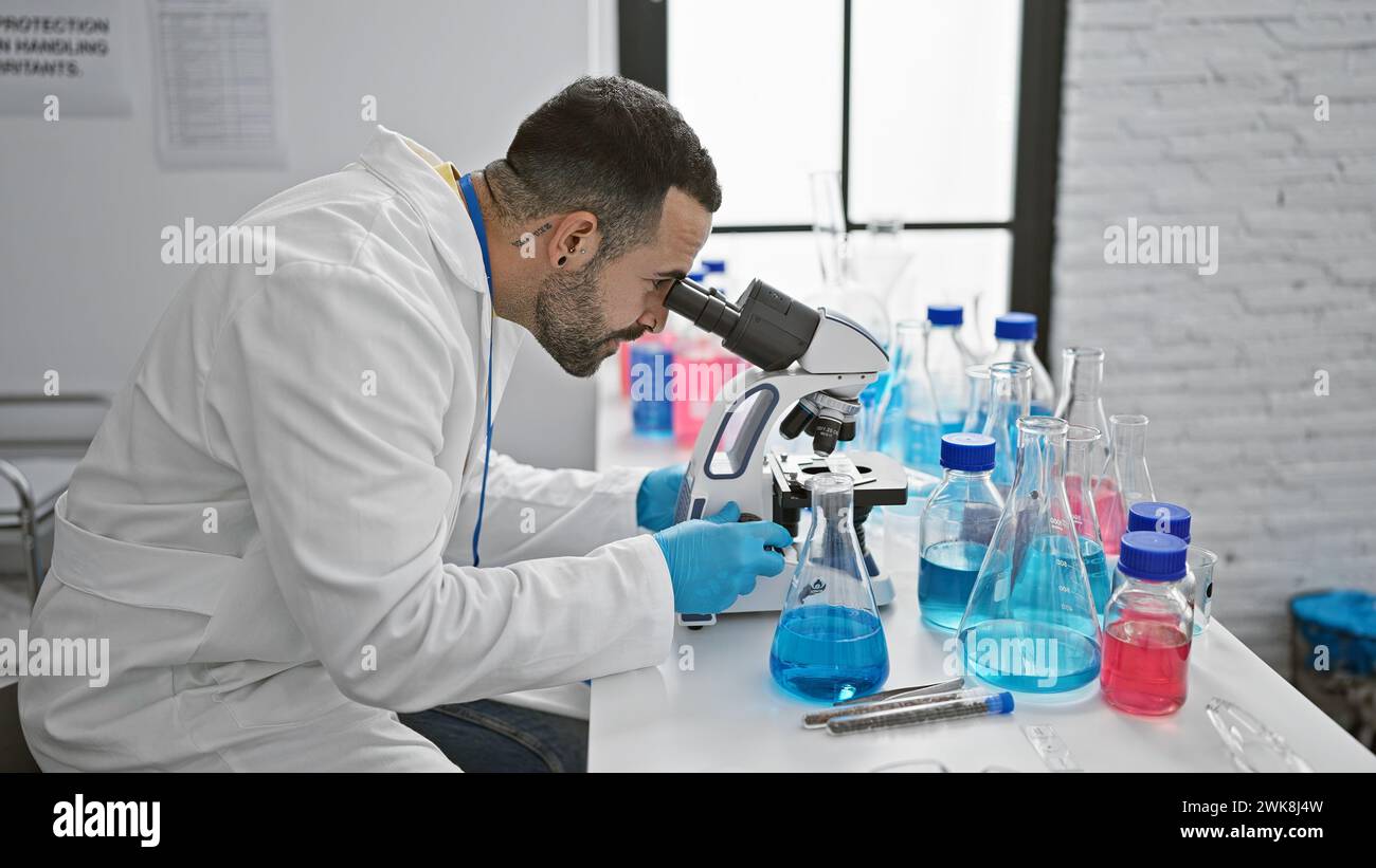 Hispanic man in lab coat analyzing samples using a microscope in a ...