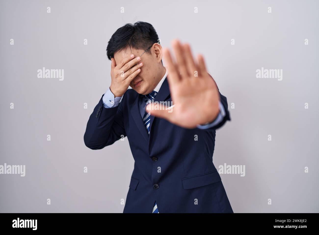 Young asian man wearing business suit and tie covering eyes with hands ...