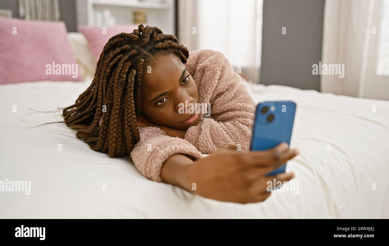African american woman with braids lying on bed using smartphone in bedroom Stock Photo - Alamy