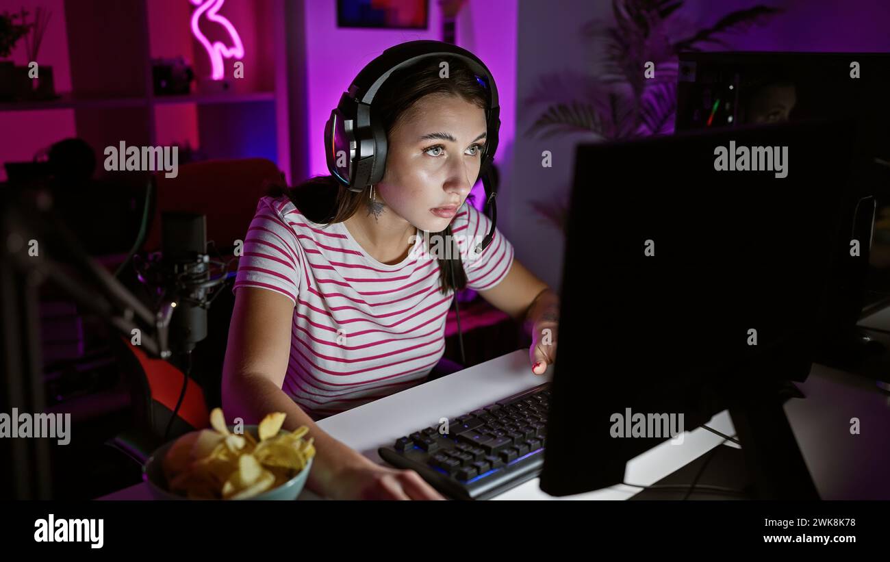 Intense young woman gaming at night in a dark room with colorful led ...