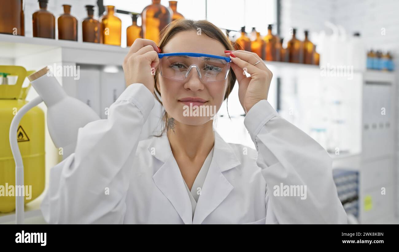 A young brunette woman scientist adjusts safety goggles in an indoor ...