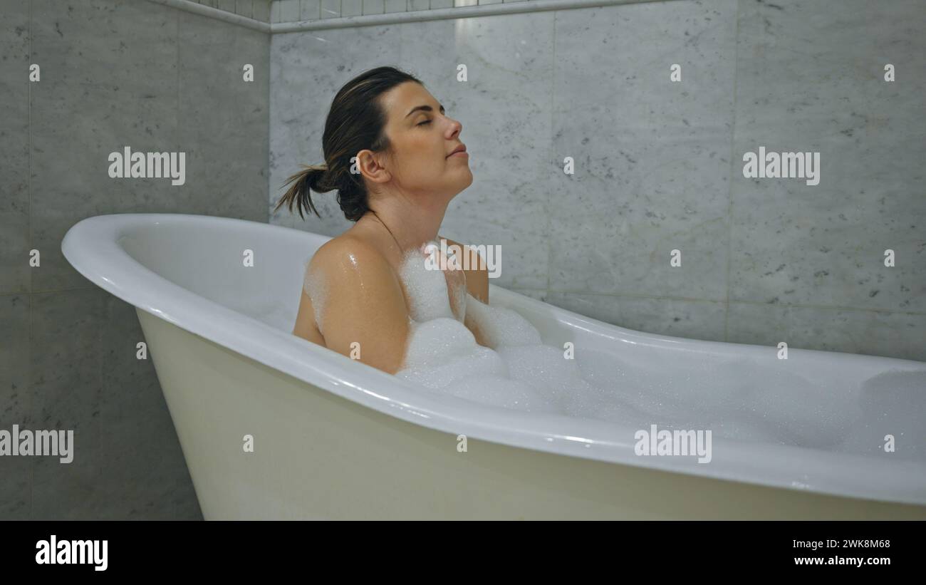 Relaxed woman enjoying a bubble bath in a white bathtub, depicting ...