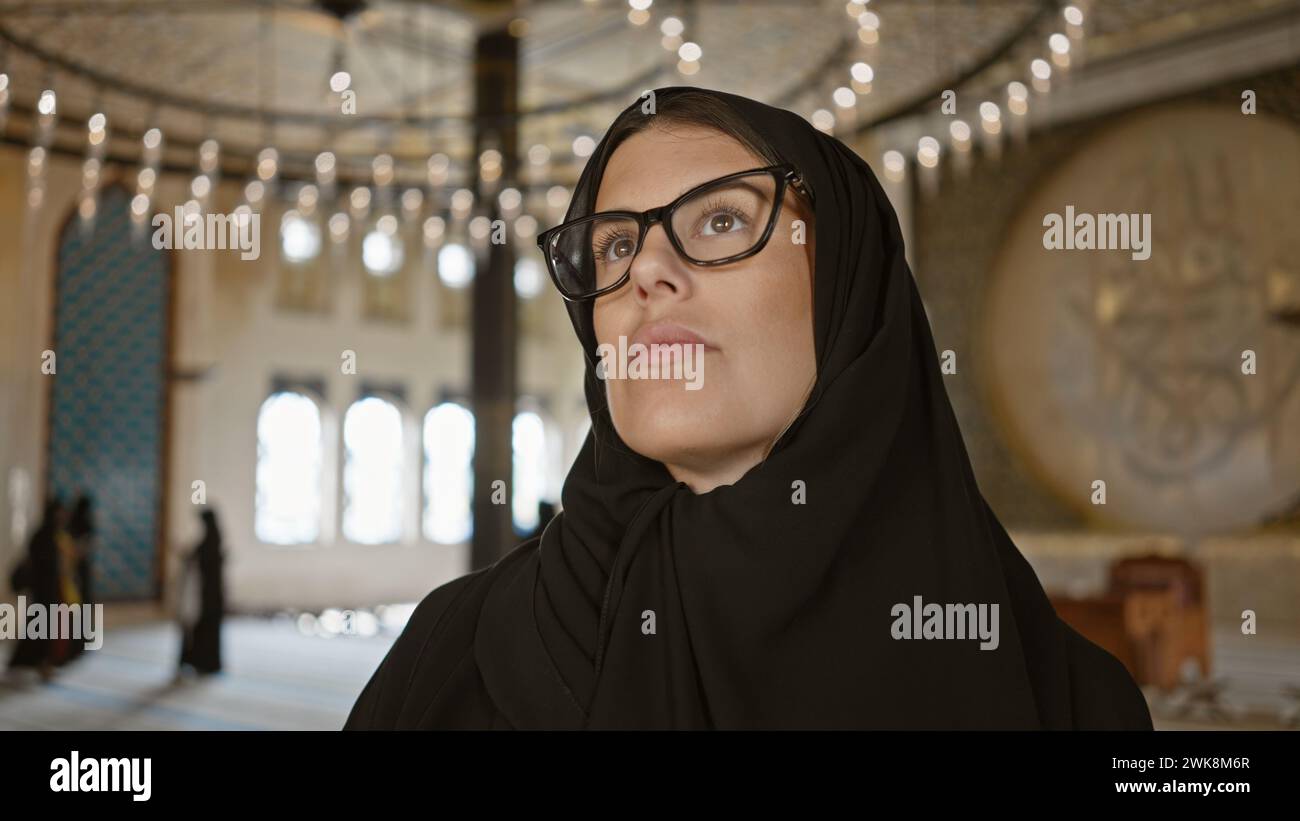 A contemplative young woman in a hijab inside a grand doha mosque ...